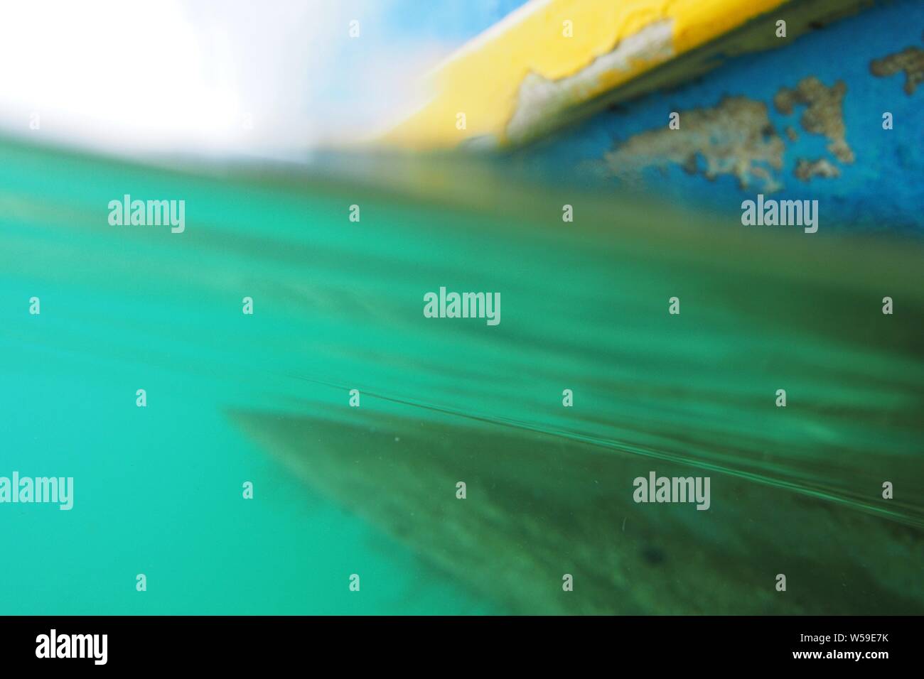 Artsy half underwater shot of a blue and yellow speedboat with peeling ...