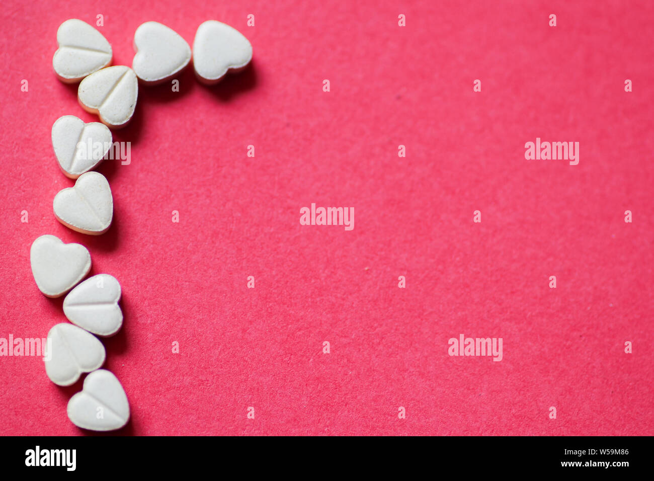heart shaped tablets stacked on a pink background with space for text ...