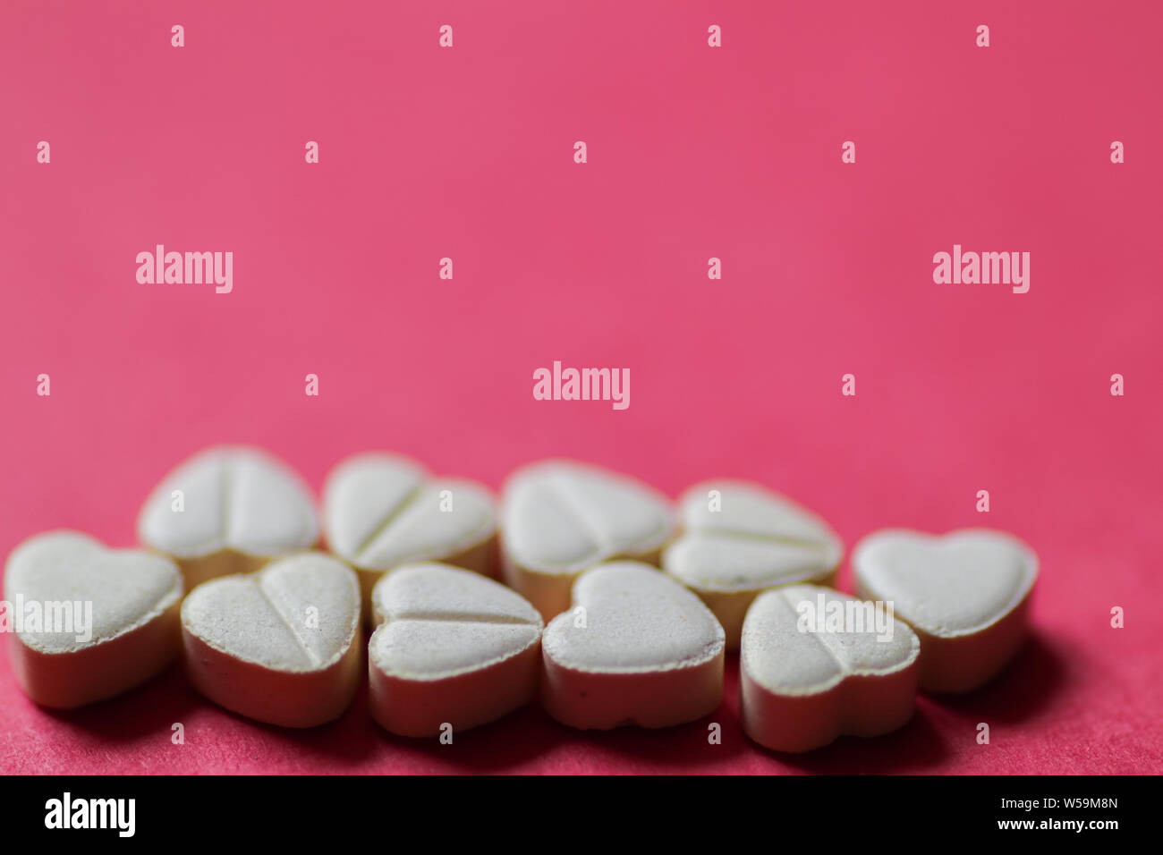 heart shaped tablets stacked on a pink background with space for text ...