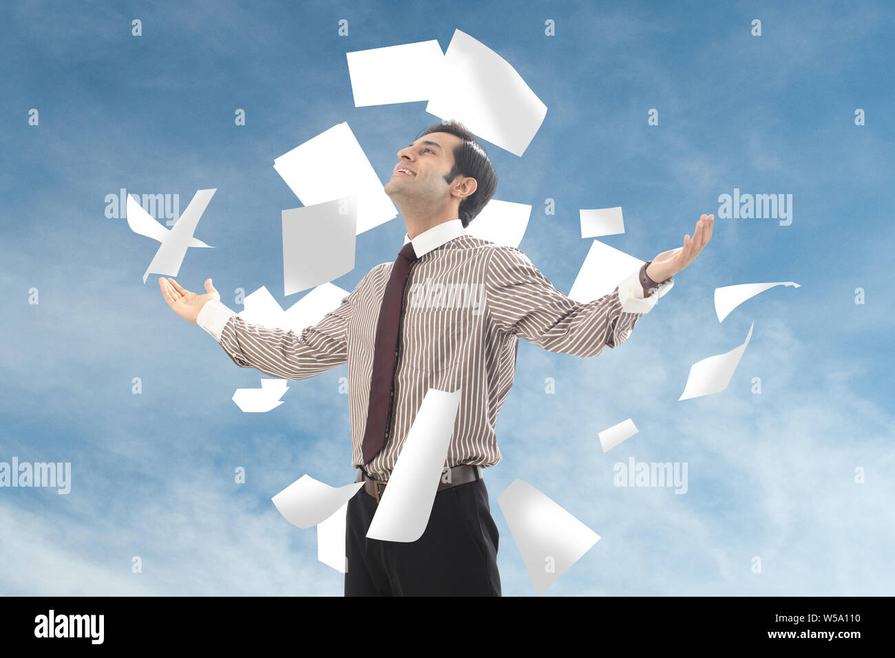 Papers falling on a businessman standing with his arms outstretched ...