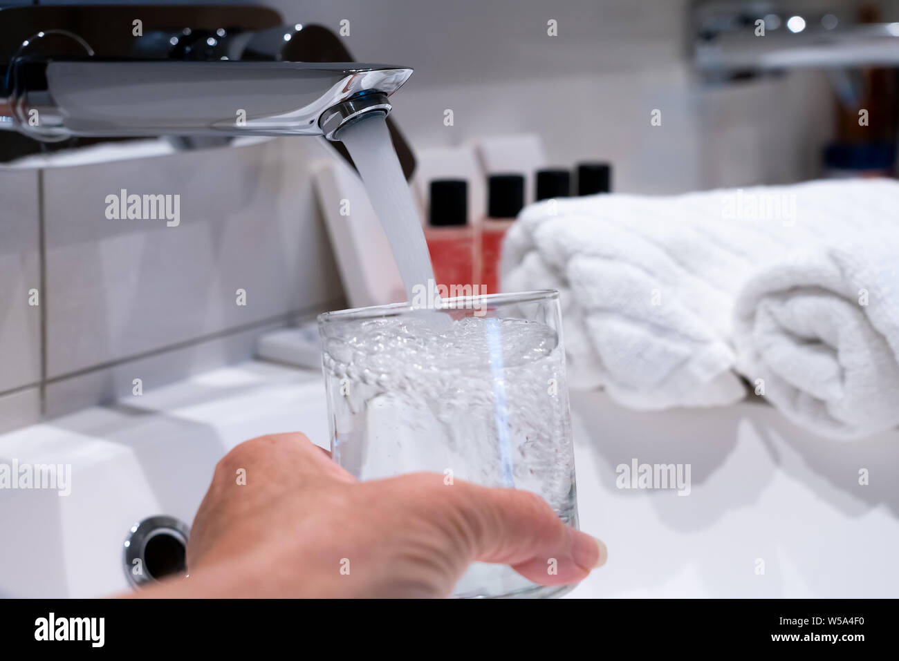 Faucet with flowing water, hand and drinking glass Stock Photo - Alamy