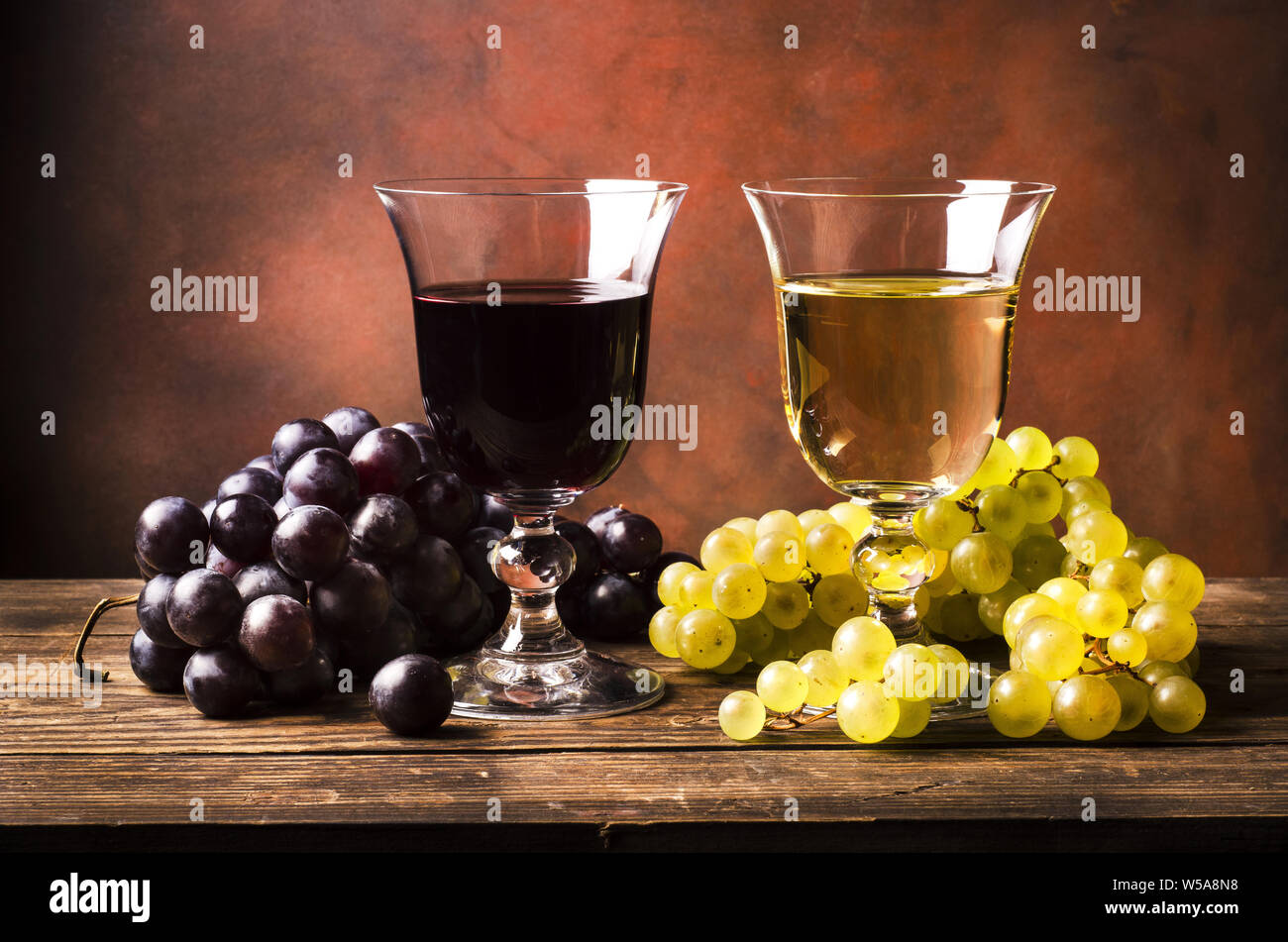 on rustic wooden table glasses of white and red wine, with mixed grapes ...