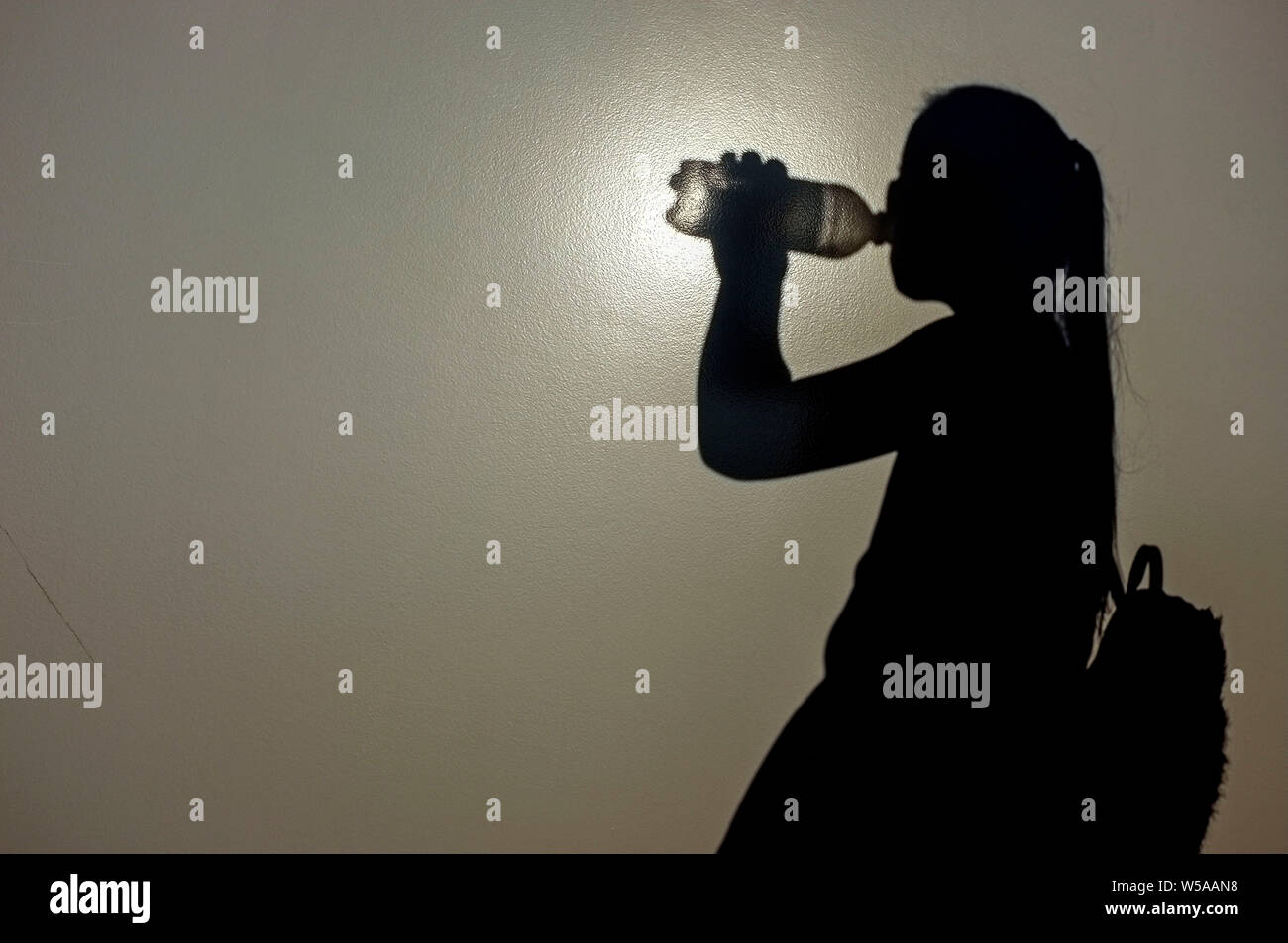 Shadow against a wall, of a young girl drinking water from a plastic ...