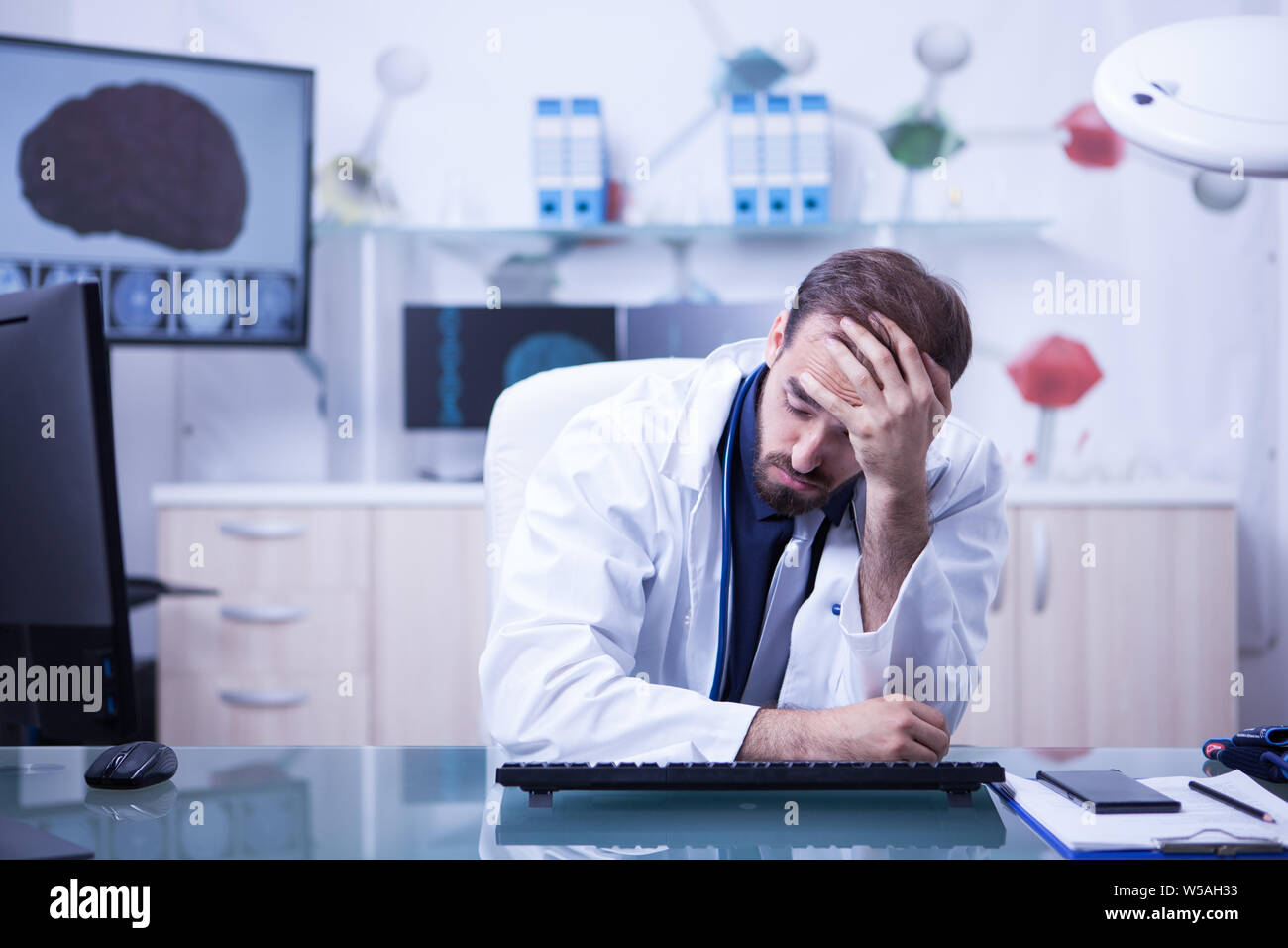 Tired young doctor trying to focus holding his head sitting down in the ...