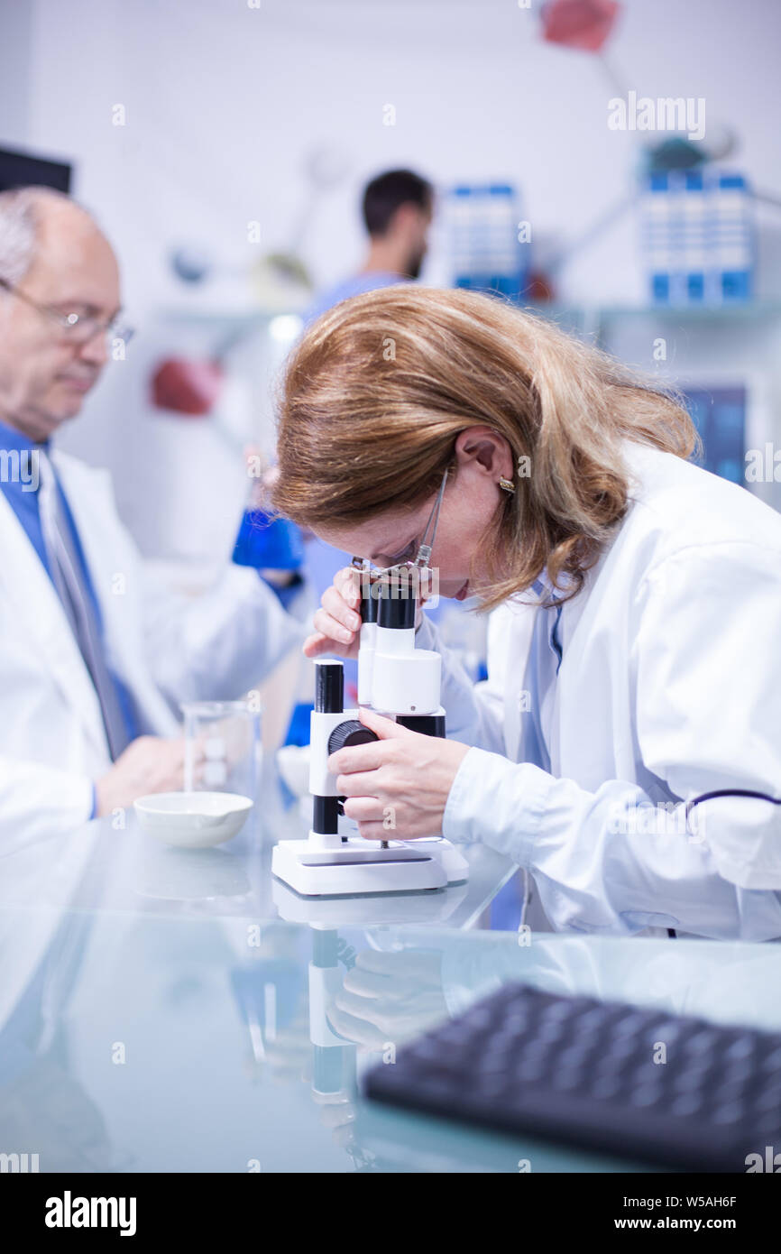 Female engineer with a white coat working under a microscope in a ...
