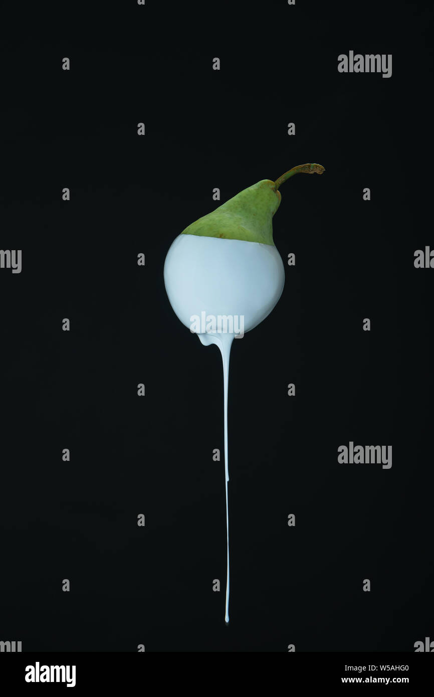 Beautiful fresh pear dripping white paint on a black background ...