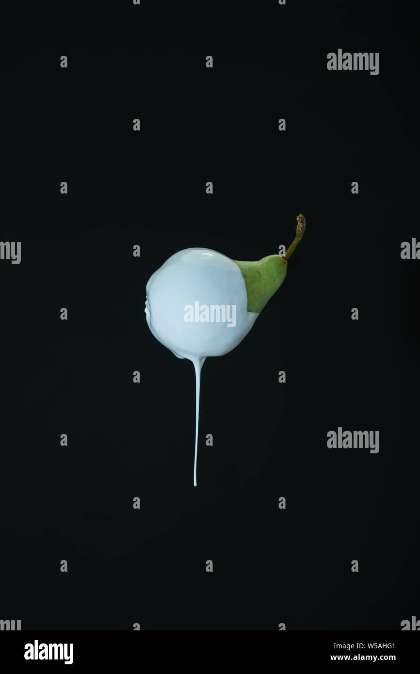 Beautiful fresh pear dripping white paint on a black background ...