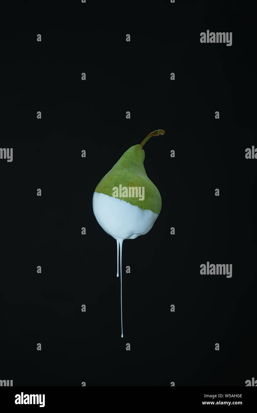 Beautiful fresh pear dripping white paint on a black background ...