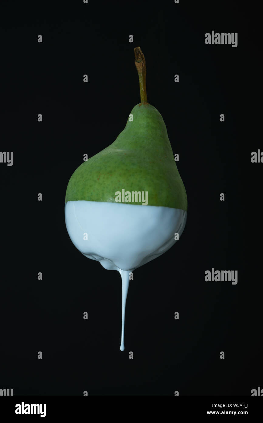 Beautiful fresh pear dripping white paint on a black background ...