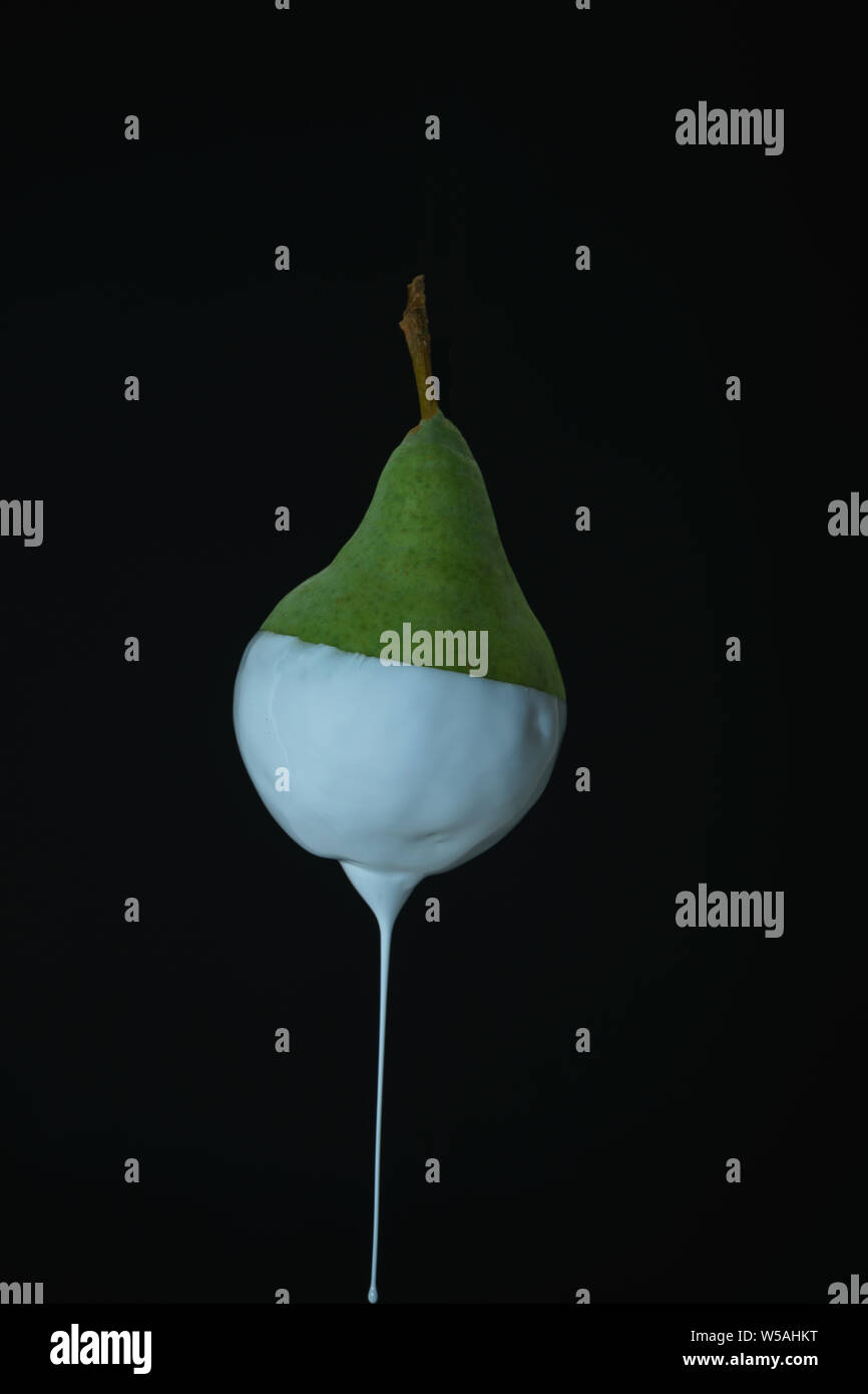 Beautiful fresh pear dripping white paint on a black background ...