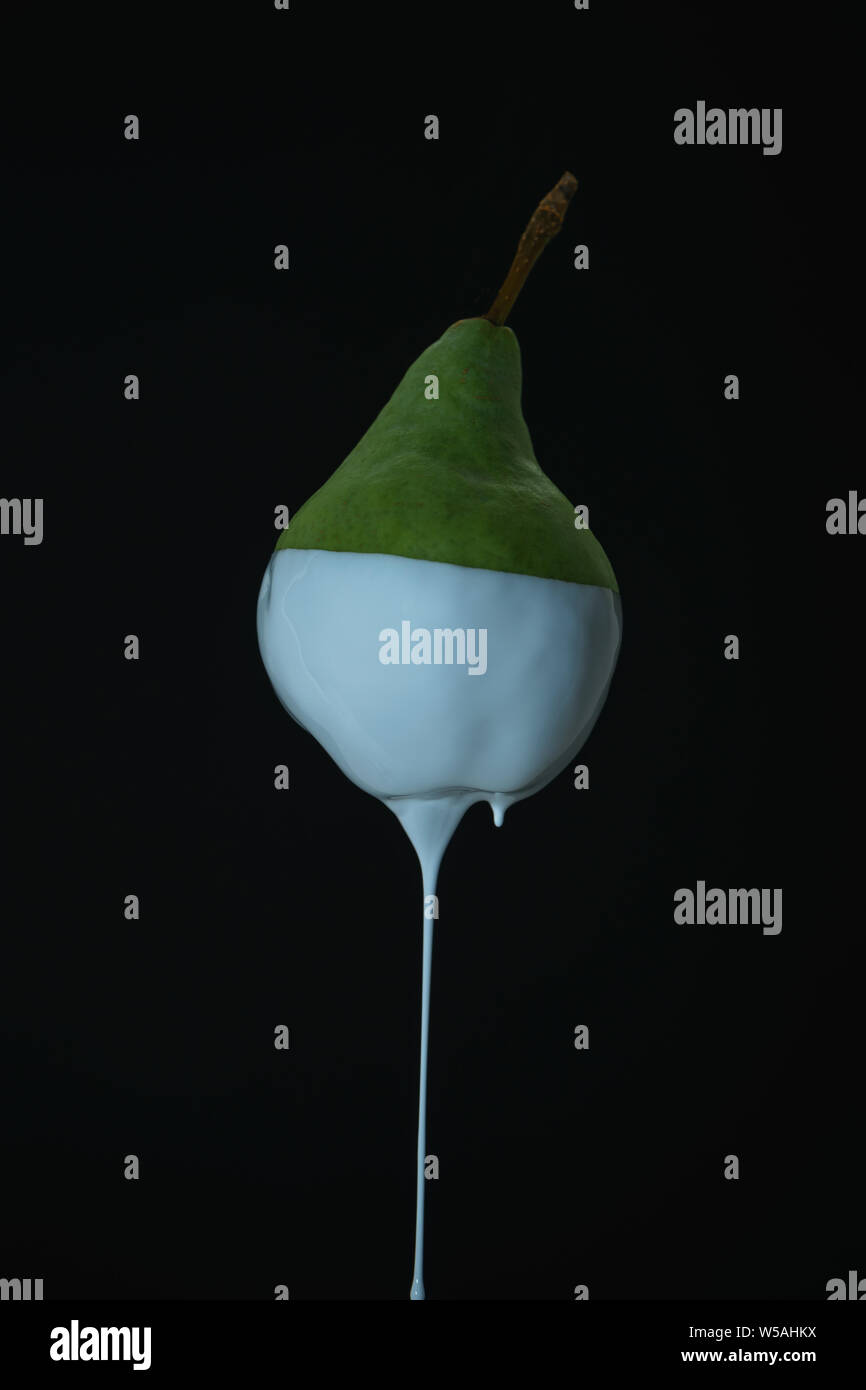 Beautiful fresh pear dripping white paint on a black background ...