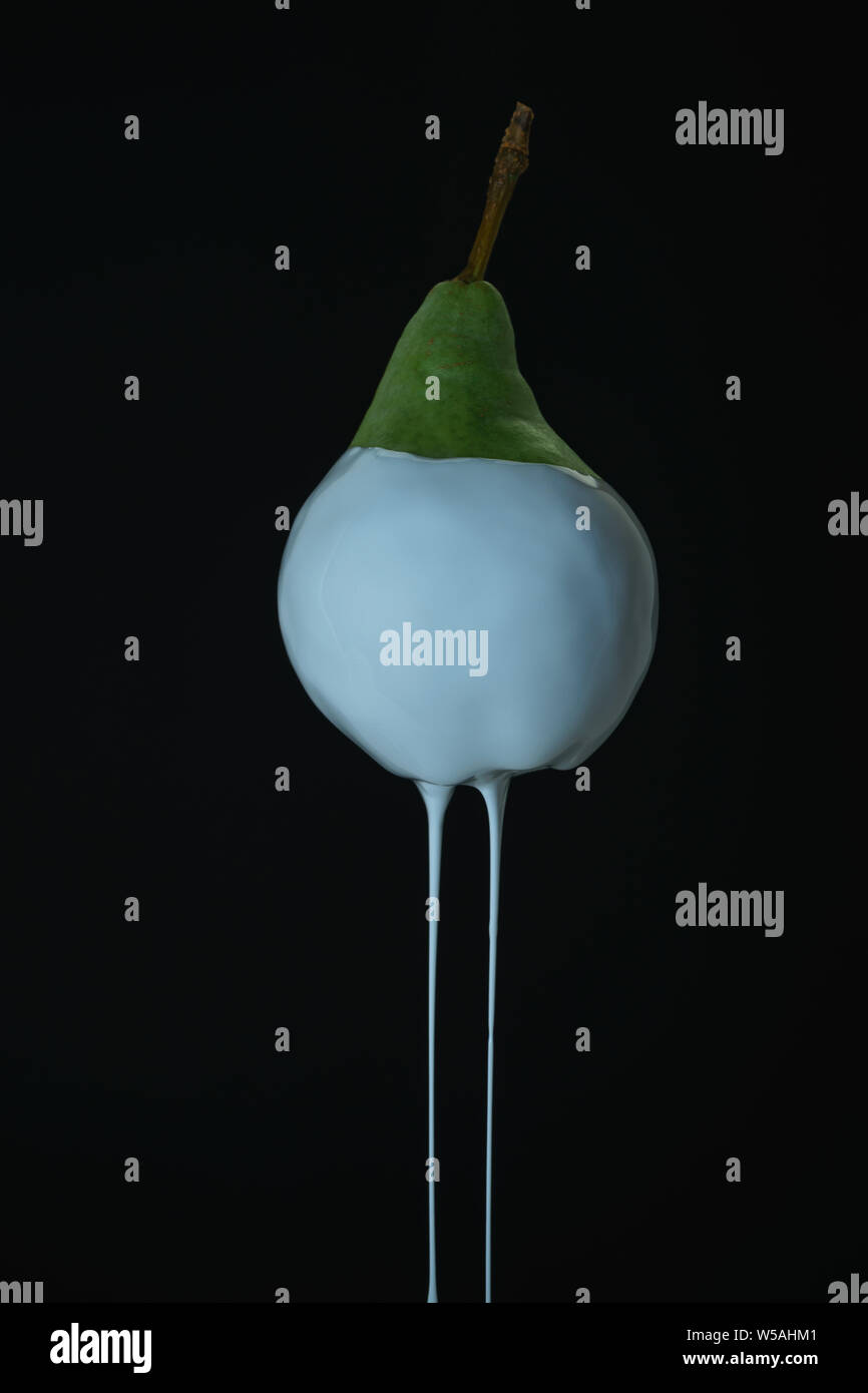 Beautiful fresh pear dripping white paint on a black background ...