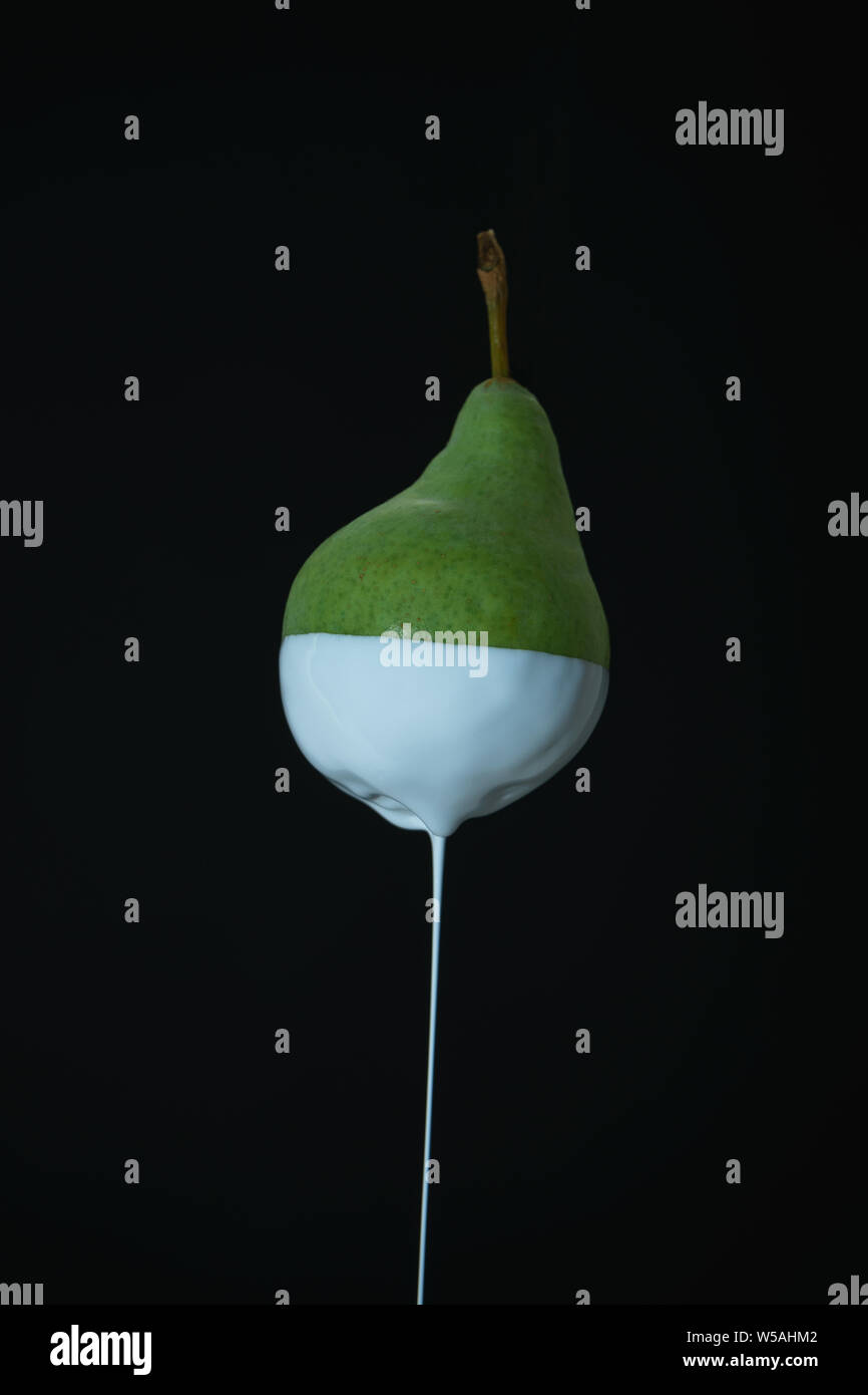 Beautiful fresh pear dripping white paint on a black background ...