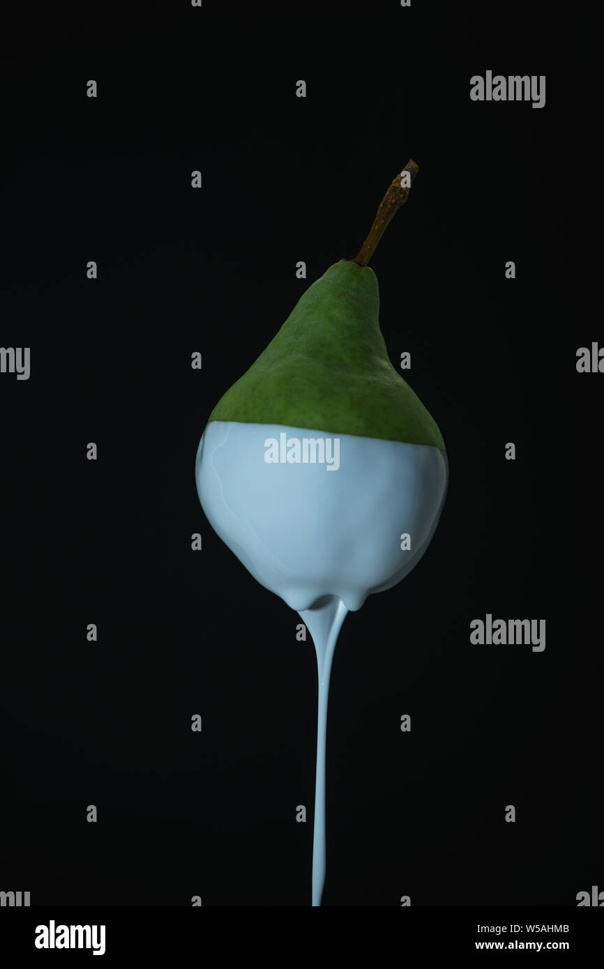 Beautiful fresh pear dripping white paint on a black background ...