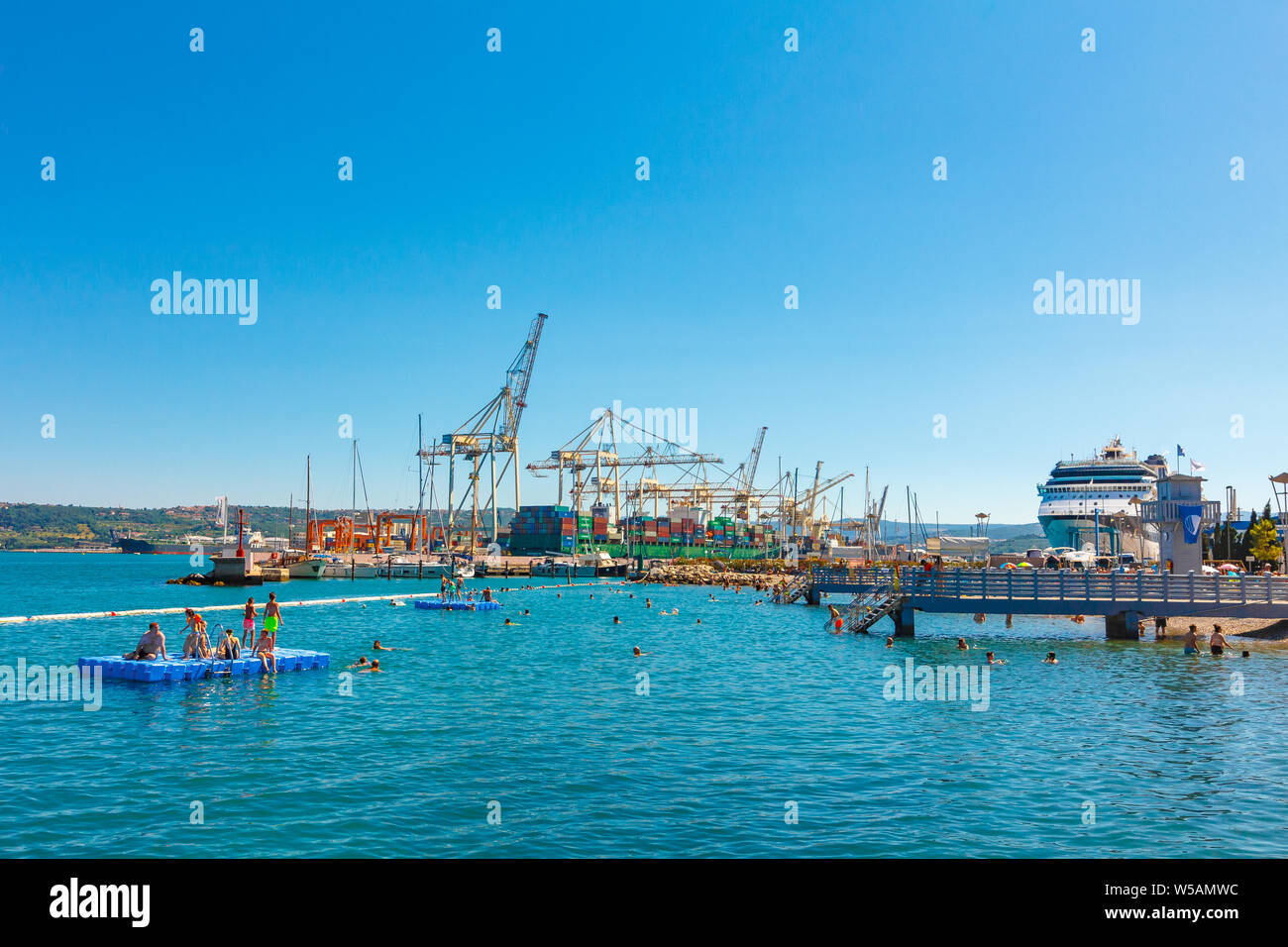 People swimming on the beach in front of harbor cranes and luxury ...