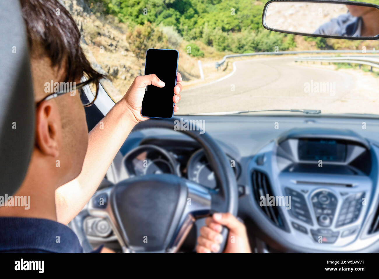 Young driver, using smartphone, on the road in the car. Distraction and ...