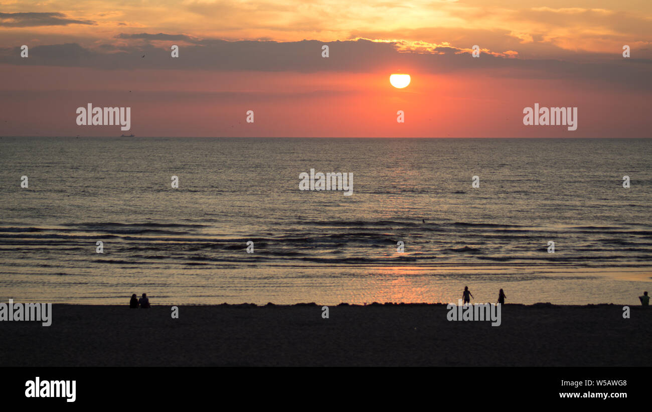 People on a beach in the evening, watching the sun going down over the sea Stock Photo - Alamy