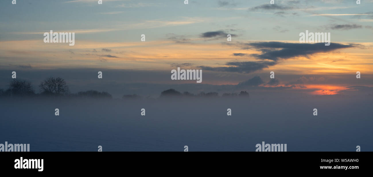 Sunset on a cold winter day, the sun behind clouds, touching the ...