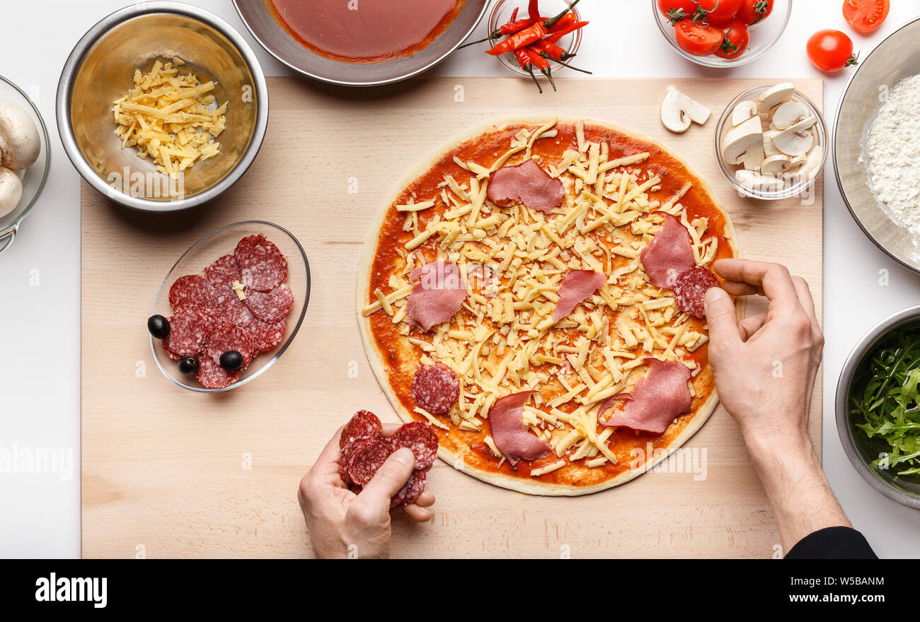 Chef decorating Italian pizza with ham and salami slices Stock Photo ...