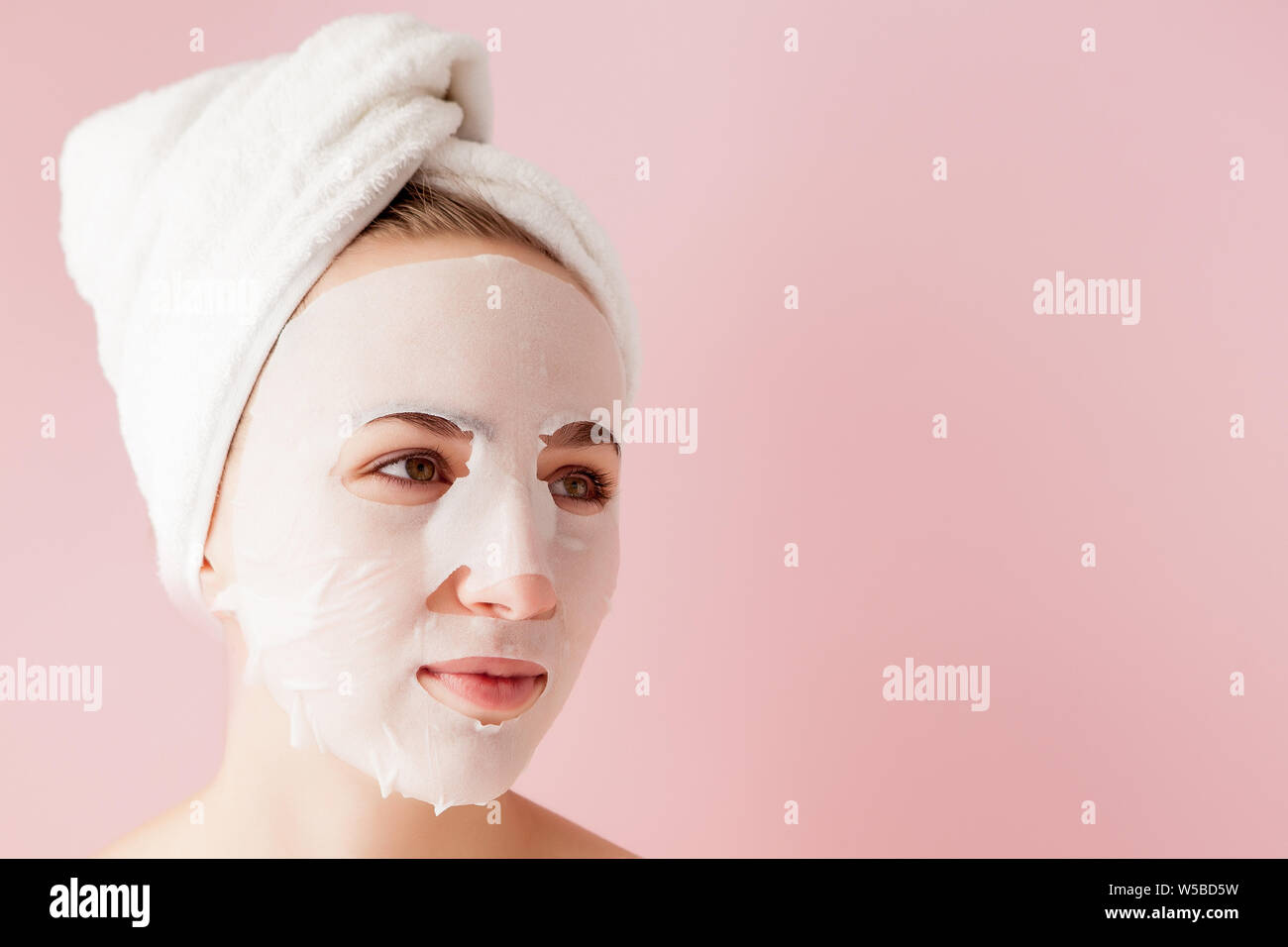 Beautiful young woman is applying a cosmetic tissue mask on a face on a ...