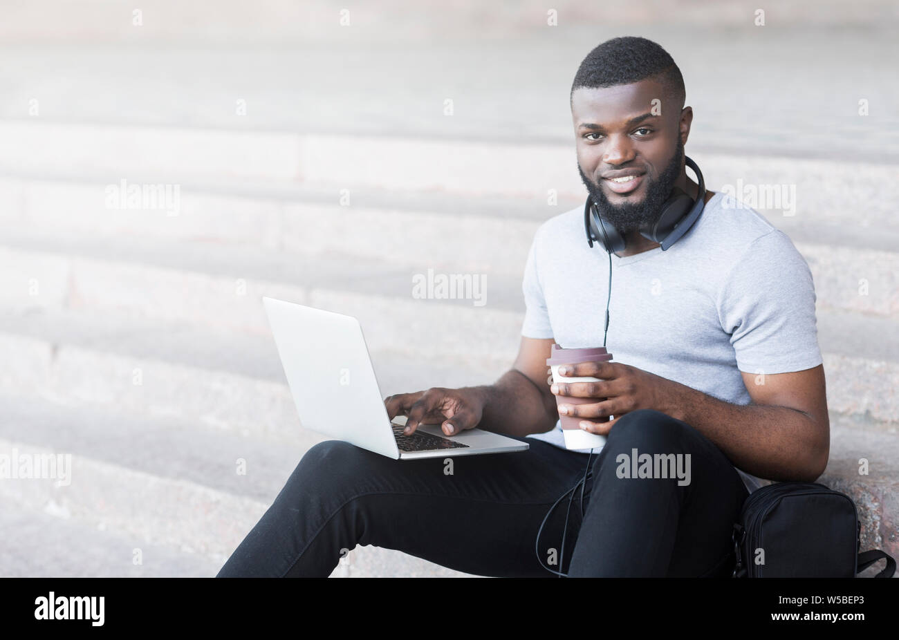 Smiling african student coding outdoor and drinking coffee Stock Photo ...