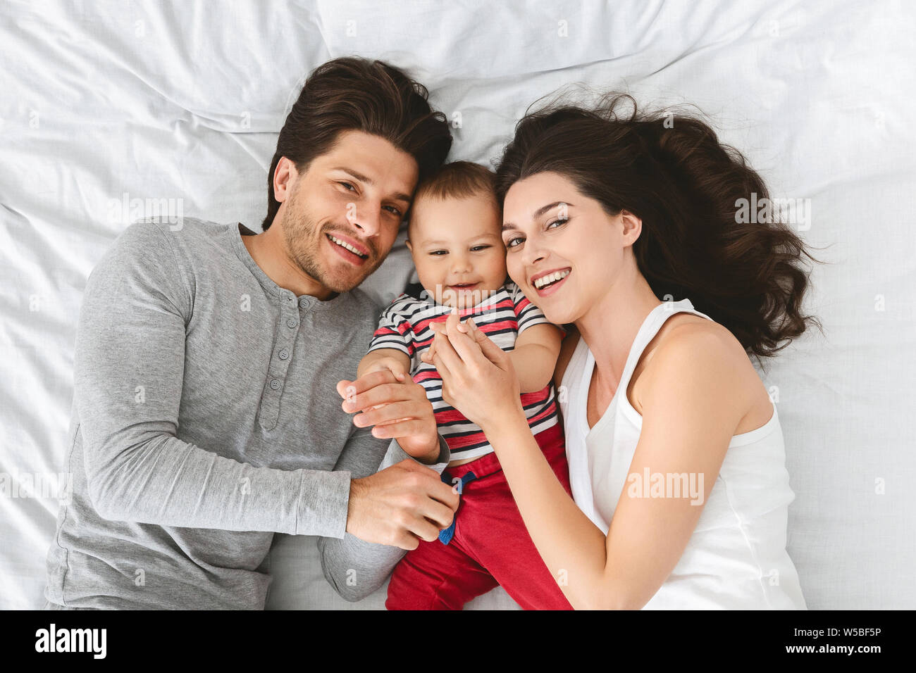 Young millennial parents embracing with baby son in bed Stock Photo - Alamy