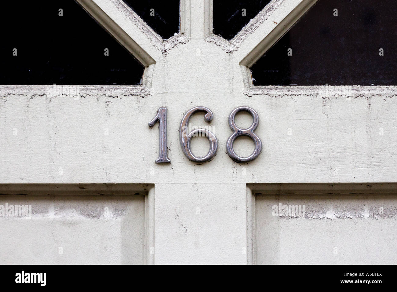 House number 168 on a dirty white wooden front door with glass inserts ...