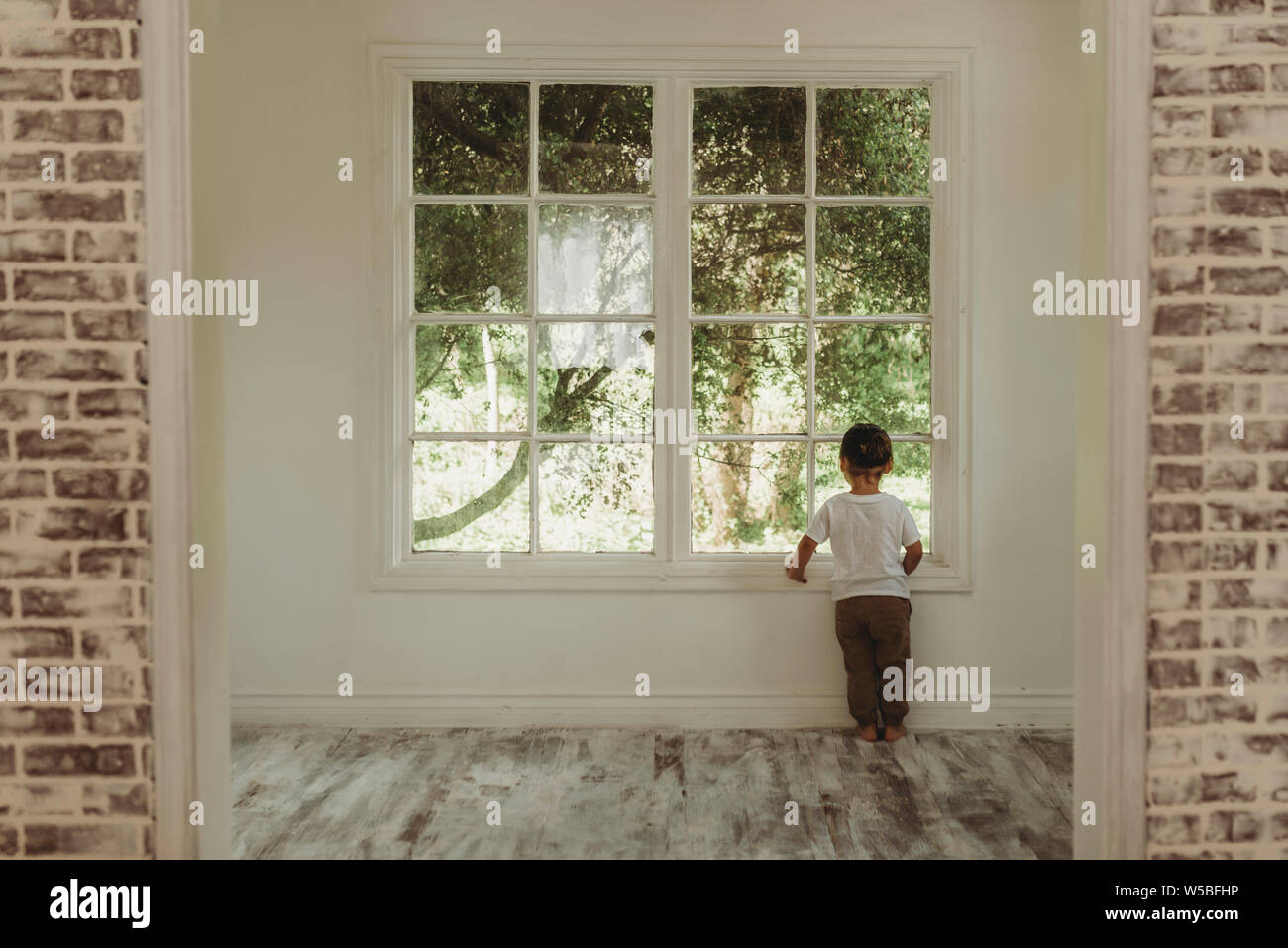 Toddler boy looking out window at trees in natural light studio Stock ...