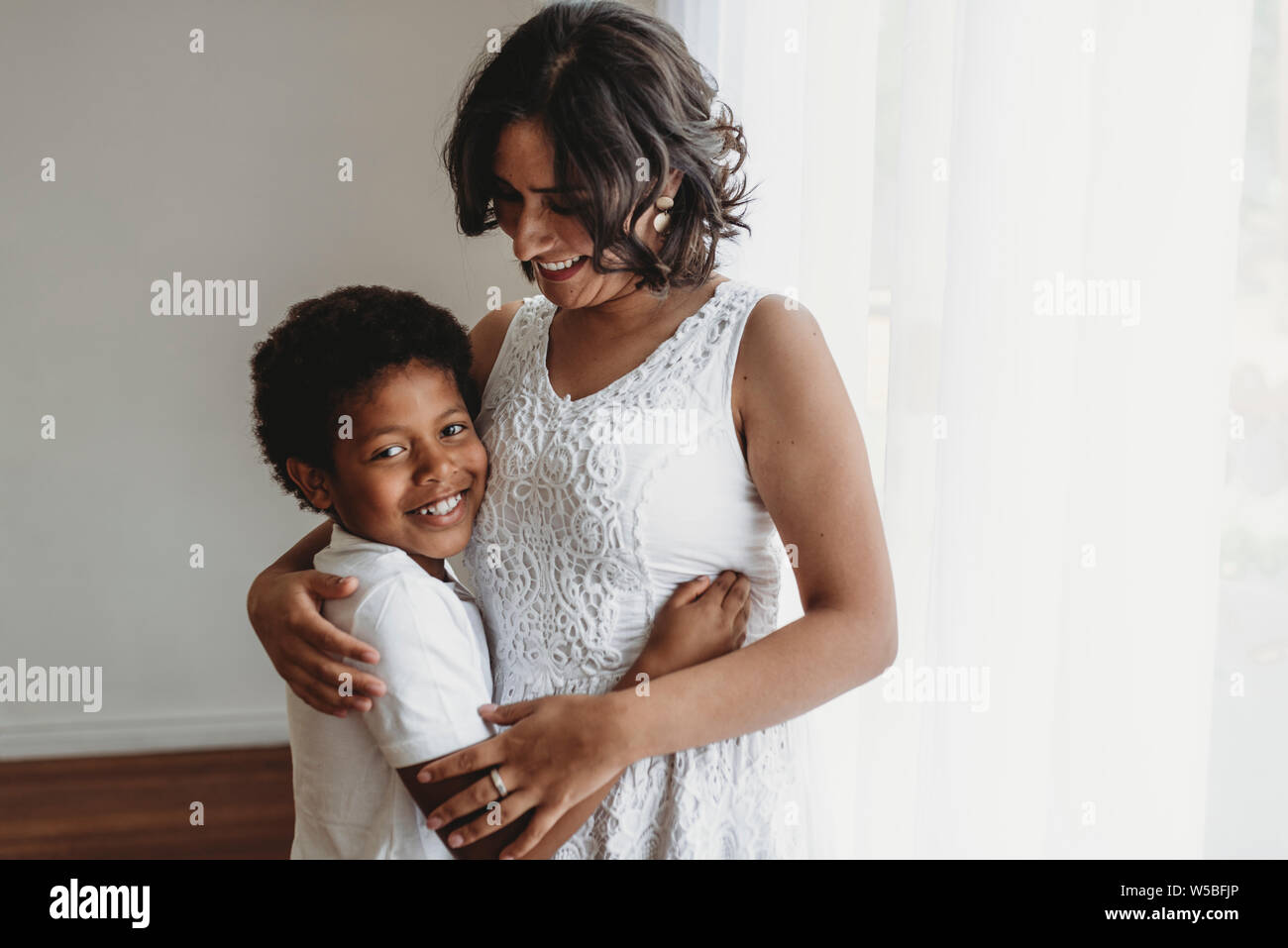 Mid-level view of smiling son being hugged by smiling mother in studio ...