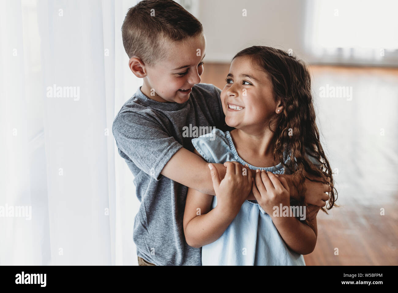 Brother and sister laughing at each other in natural-light studio Stock ...