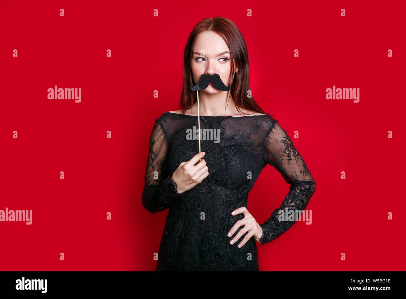 Surprised pretty young woman holding funny mustache on stick. Joyful ...