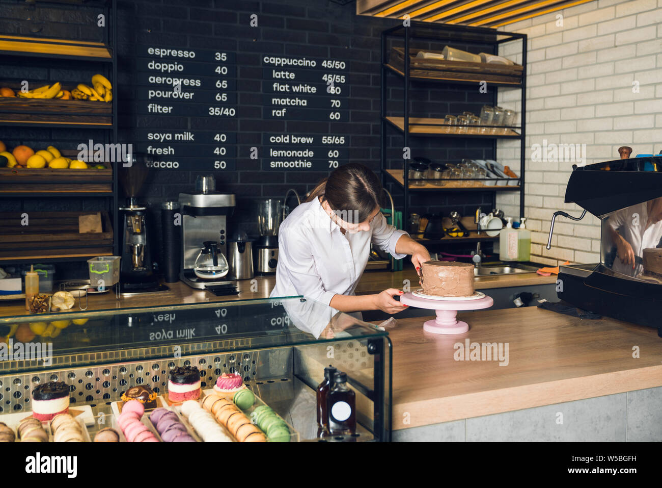 Woman bake and decorate chocolate cake in cafeteria near the showcase ...