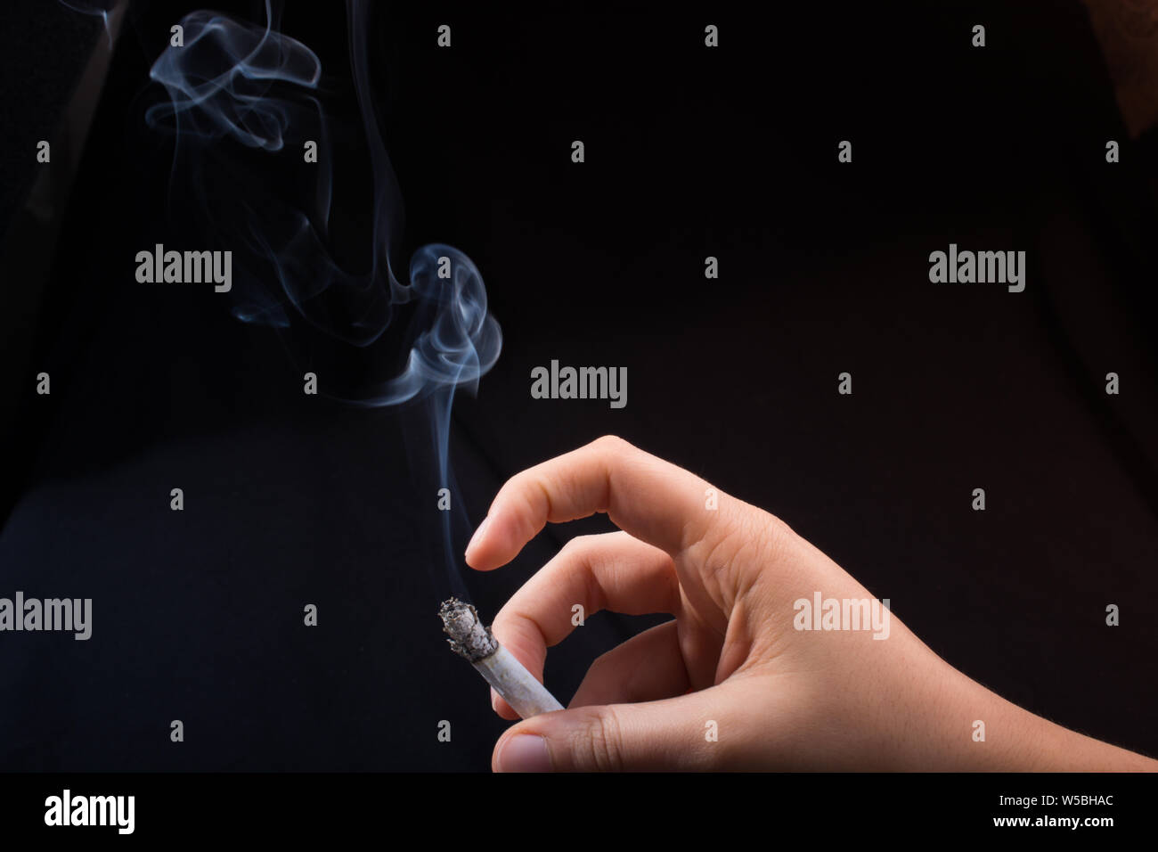 Hand is holding smoking cigarette with smoke around Stock Photo - Alamy
