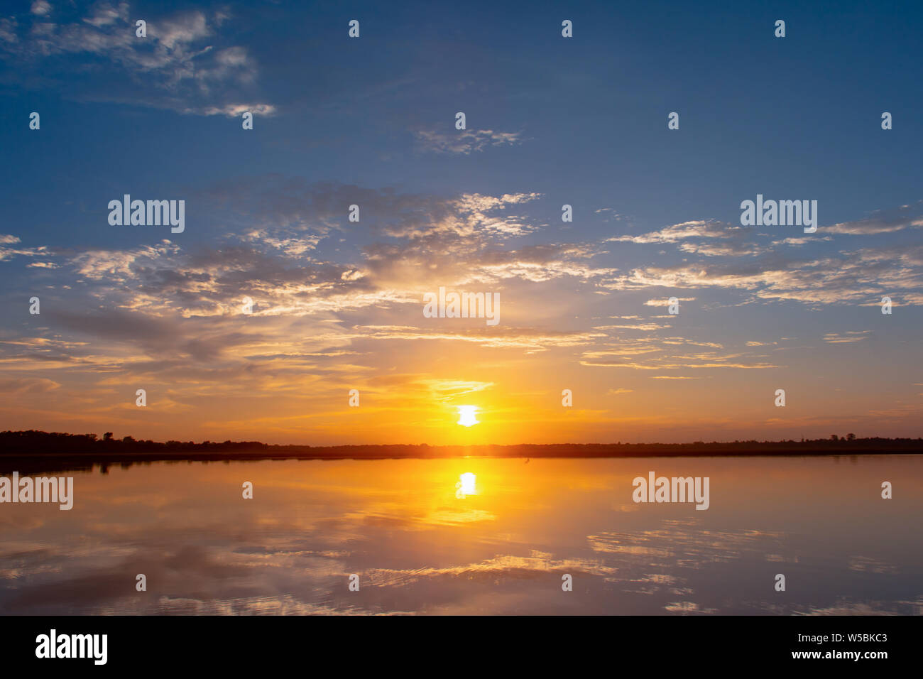 Sunset reflection lagoon. beautiful sunset behind the clouds and blue sky above the over lagoon ...