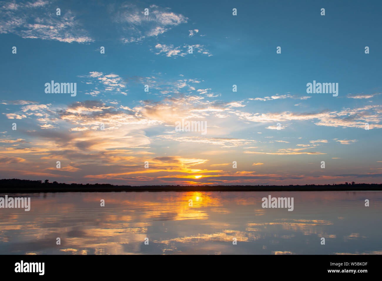 Sunset reflection lagoon. beautiful sunset behind the clouds and blue sky above the over lagoon ...