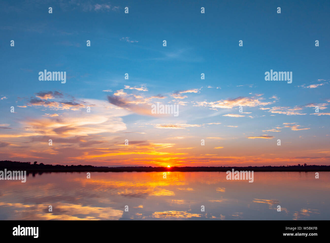 Sunset reflection lagoon. beautiful sunset behind the clouds and blue sky above the over lagoon ...