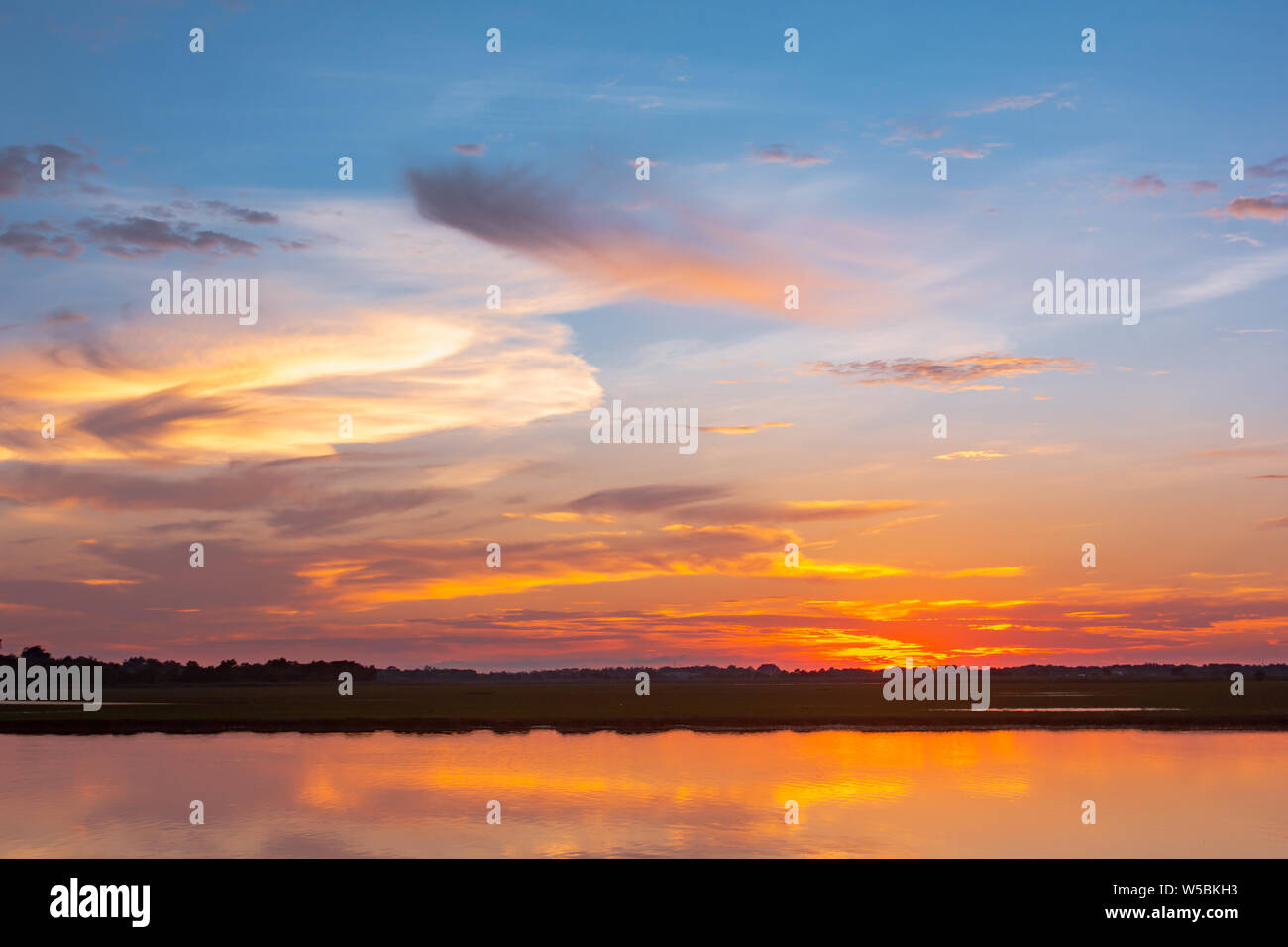 Sunset reflection lagoon. beautiful sunset behind the clouds and blue sky above the over lagoon ...