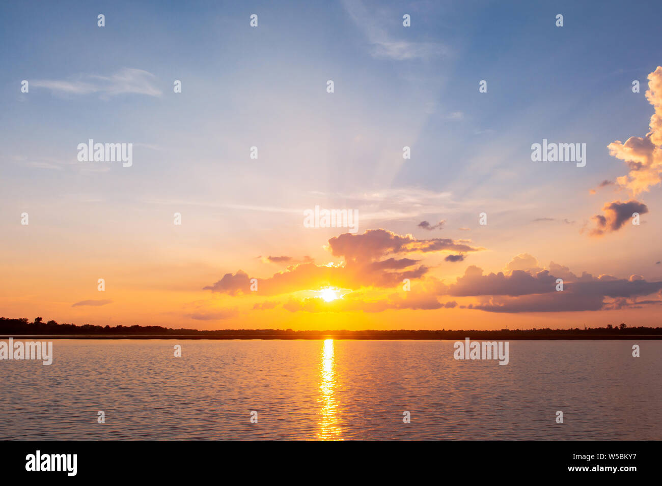 Sunset reflection lagoon. beautiful sunset behind the clouds and blue sky above the over lagoon ...
