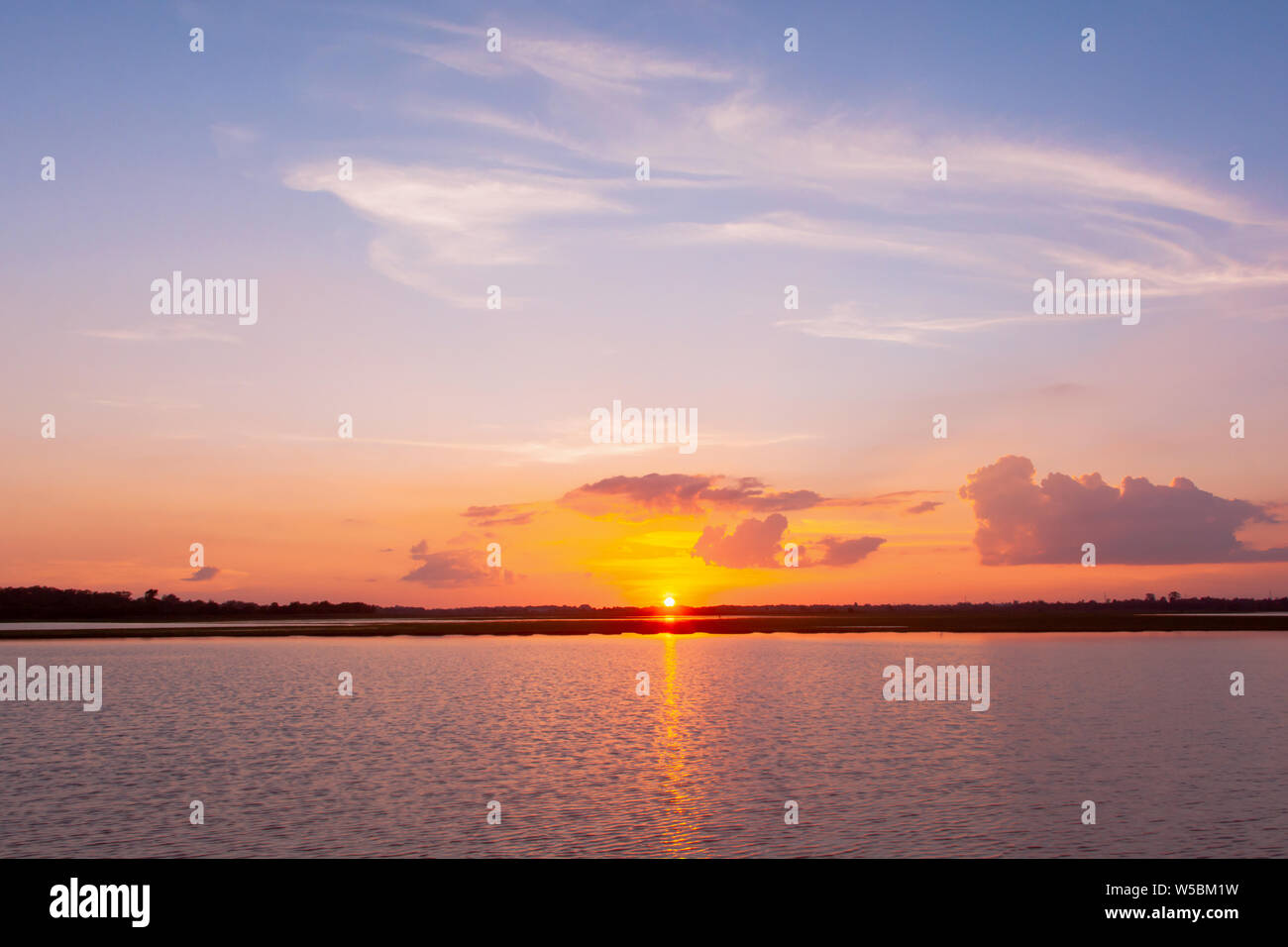Sunset reflection lagoon. beautiful sunset behind the clouds and blue sky above the over lagoon ...