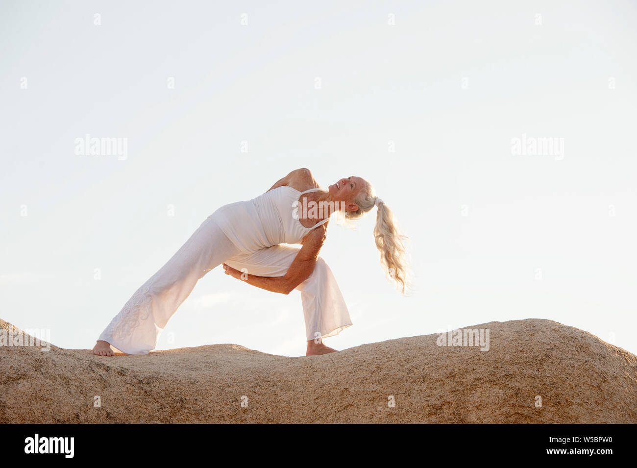 Senior woman in yoga pose on the rocks Stock Photo - Alamy