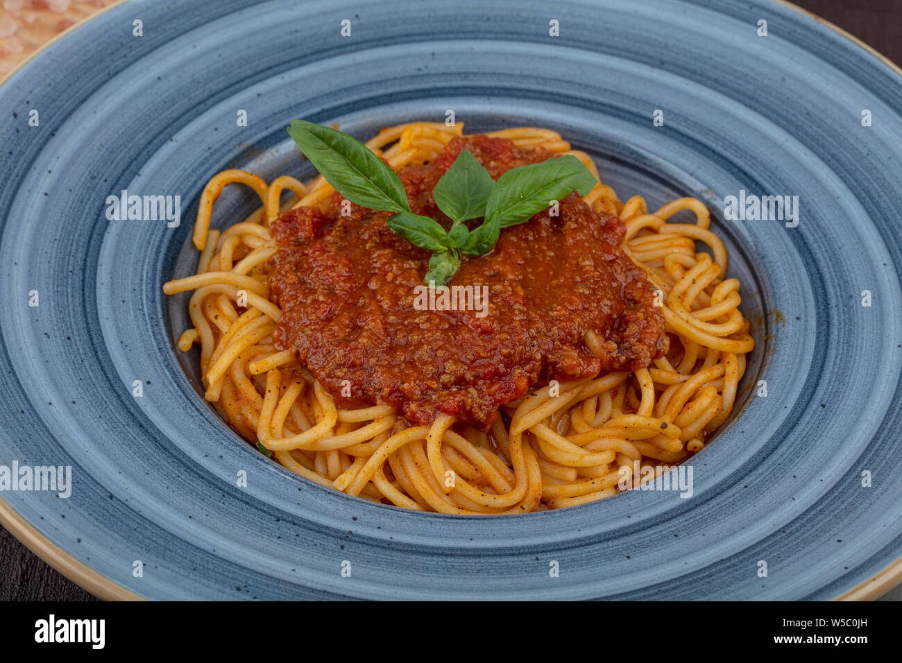 Spaghetti bolognese in a blue plate on a dark wood background.Top view ...