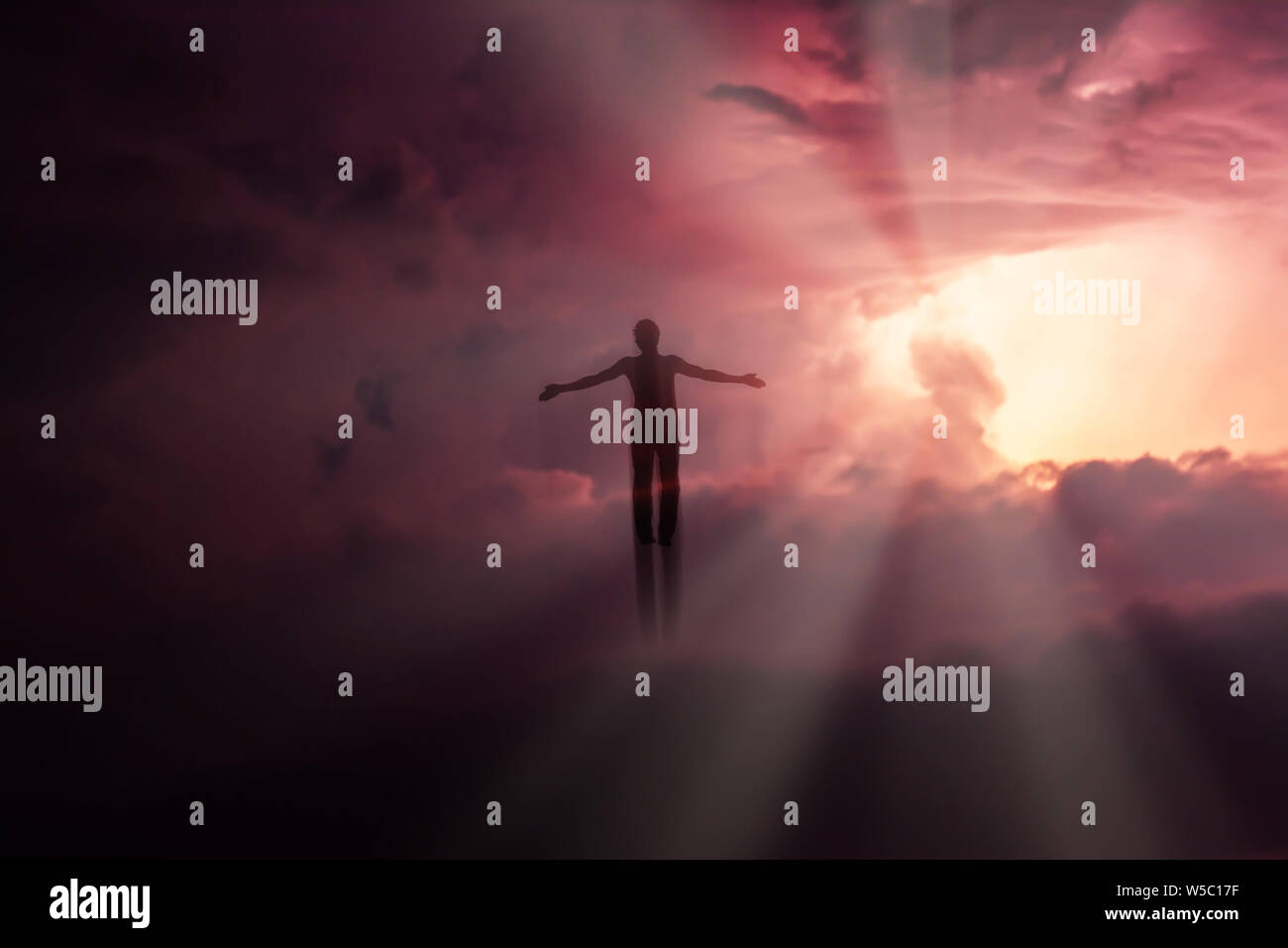 Silhouette of a man flying up in the sky in the bright rays of the sun ...