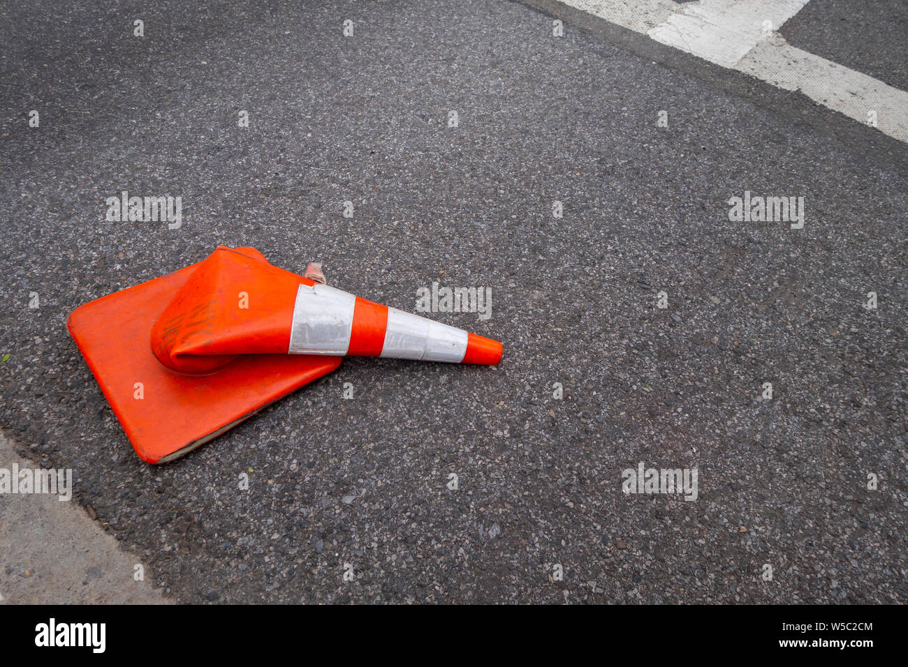 White reflective striped orange cone crushed by a car on the street ...