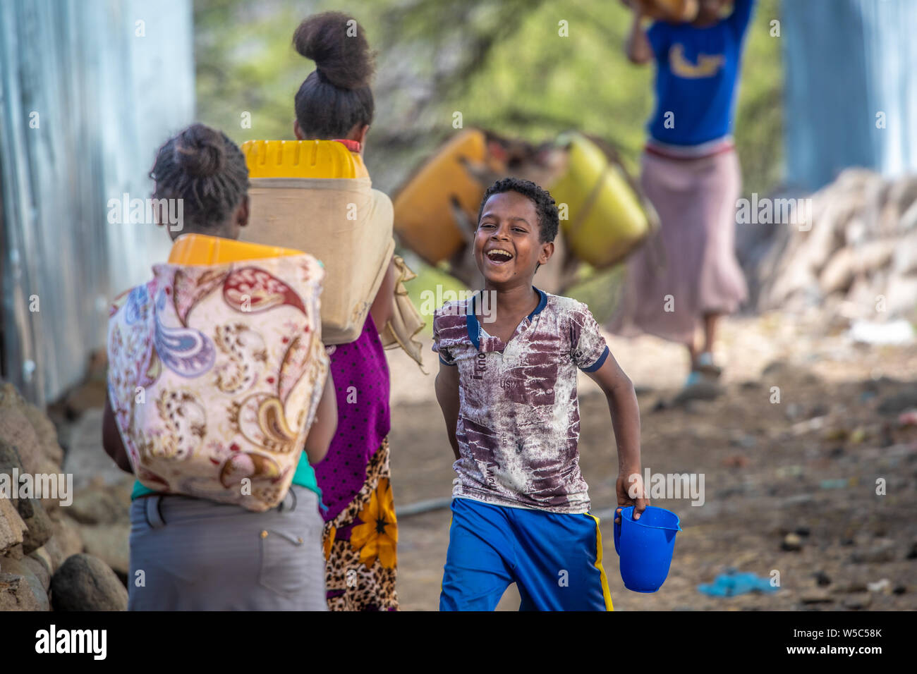 A young boy walks down a street smiling jovially past women carrying ...