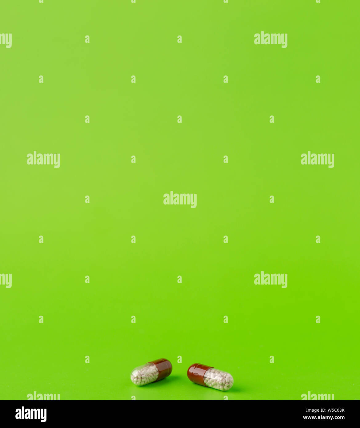 Two brown capsules with medicinal microgranules on a green background ...
