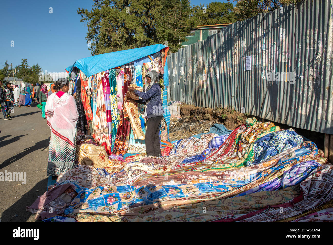A shopkeeper arranges textiles and other fabrics for sale at a street ...