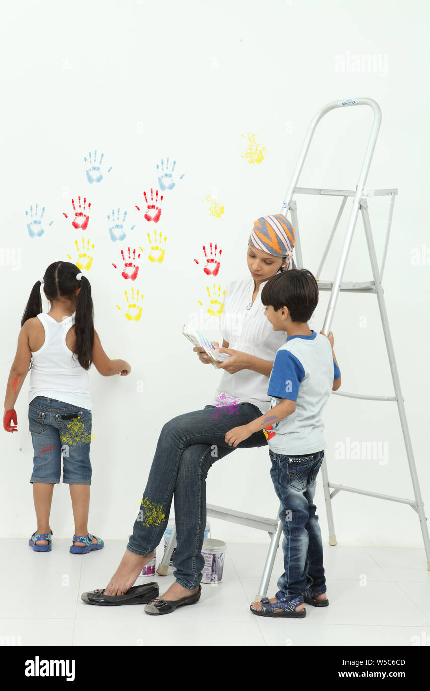 Girl painting handprints on wall with her mother and brother behind her ...