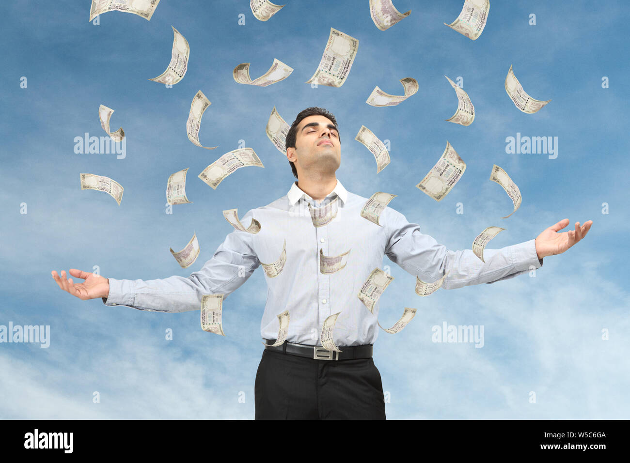 Money falling on a businessman standing with his arms outstretched ...