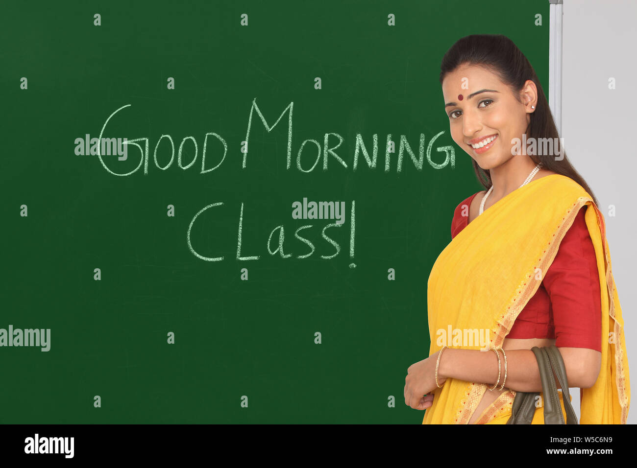 Female teacher smiling with good morning class written on a blackboard ...