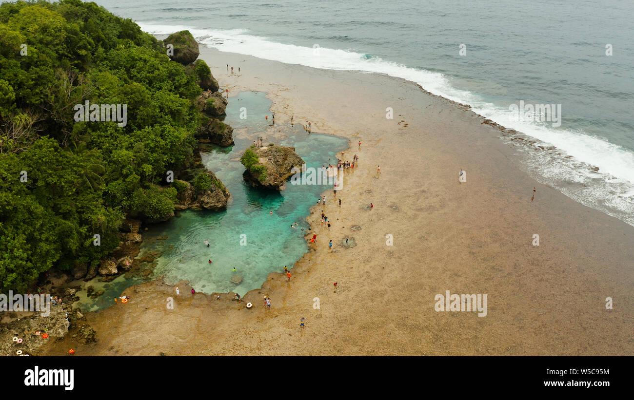 Rocky shore at low tide with swimming pools and tourists. Magpupungko ...